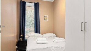 Um quarto com cama, guarda-roupa, janela com cortinas, radiador e luz no teto.