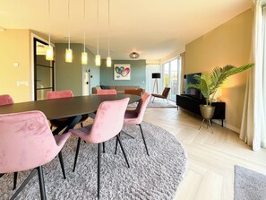 Uma sala de estar moderna com área de jantar, uma planta em vaso grande e uma televisão de tela plana.