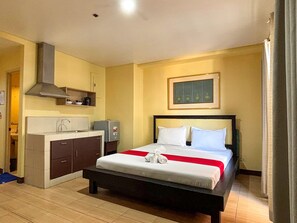 Quarto de hotel com cama, cozinha compacta, pintura na parede e janela com cortinas.