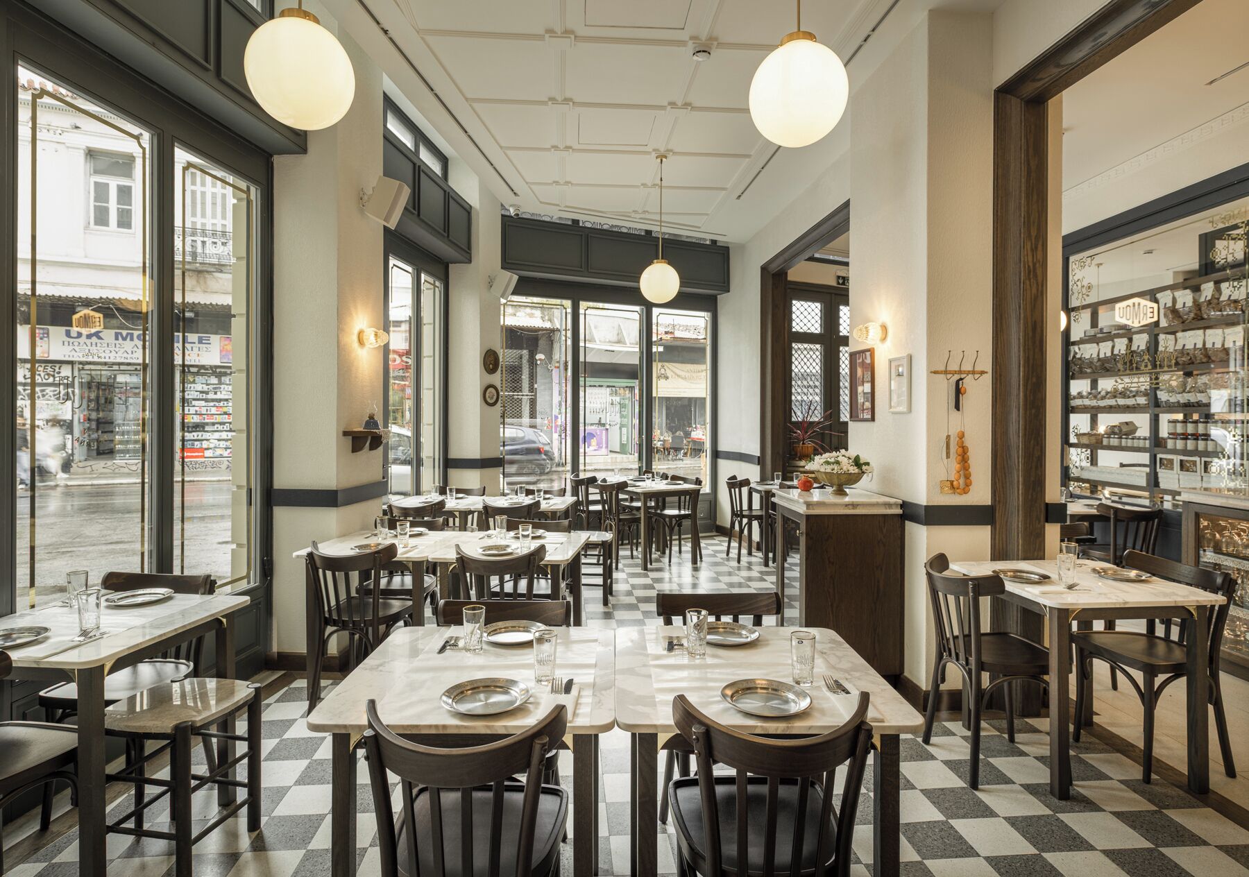 Interior de restaurante com chão xadrez, mesas postas com pratos e copos, e luminárias pendentes.