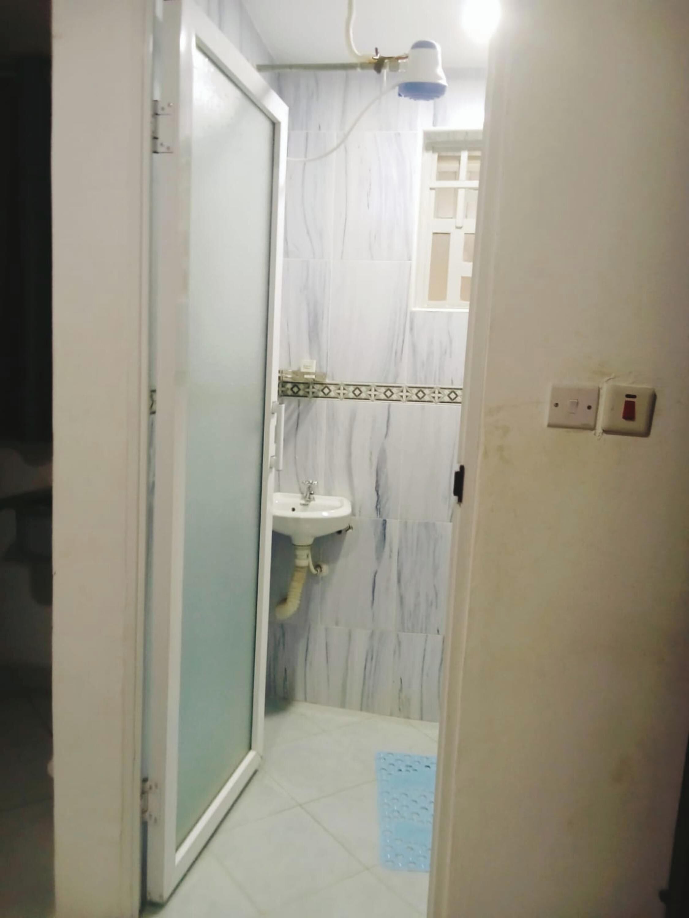 Um banheiro com pia branca, paredes com padrão marmorizado, piso ladrilhado e porta que dá para outro cômodo.