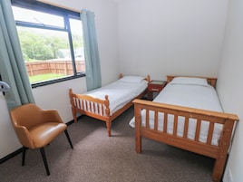 Quarto com duas camas de madeira, uma cadeira e janela com cortinas.