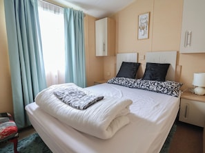 Quarto de hotel com cama, mesa de cabeceira, luminária, janela com cortinas e um quadro na parede.