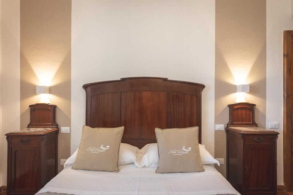Quarto com cabeceira de madeira, duas mesas de cabeceira e duas almofadas com logotipo.