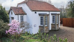Um edifício branco com telhado de telhas vermelhas, molduras de janela de pedra e uma placa indicando 'Little House Lodge'.