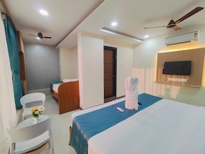 Quarto de hotel com cama, escrivaninha, cadeira, televisão e ventoinha no teto.