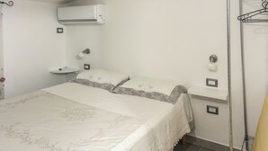 Quarto com cama, ar condicionado, prateleira na parede e cabideiro.