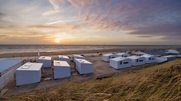 Um hotel à beira-mar com várias cabanas brancas, vista para a praia e um pôr do sol ao fundo.