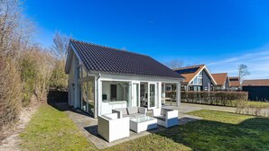 Uma casa moderna com varanda coberta, área de estar externa e gramado bem cuidado.