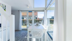 Uma cozinha moderna com armários brancos, uma mesa de jantar com cadeiras brancas e grandes janelas com vista para o exterior.