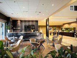 Um lobby moderno de hotel com área de bar, espaços para sentar e balcão de recepção.