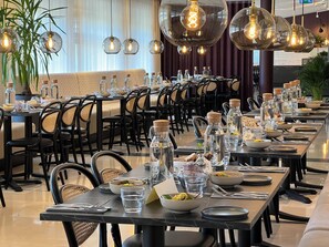 Restaurante com mesas compridas, cadeiras pretas e luminárias pendentes.