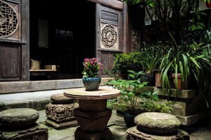 Pátio com mesa de pedra, plantas em vasos e arquitetura de madeira tradicional.