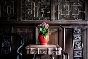 Uma mesa de madeira com um vaso vermelho contendo flores, posicionada diante de uma parede com detalhes entalhados.