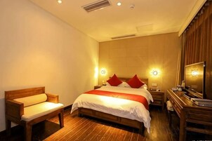 Quarto de hotel com uma cama grande, mesas de cabeceira, um banco de madeira e um espelho.