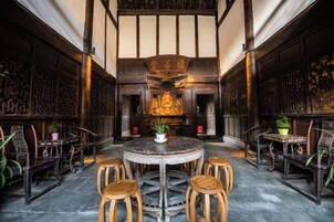 Um interior tradicional com uma mesa redonda rodeada por banquetas de madeira, um elemento decorativo central e paredes com padrão.
