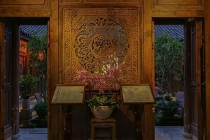 Uma porta de madeira tradicional com entalhes elaborados, um vaso de plantas e uma pequena mesa com um aviso.