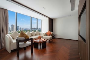 Uma sala de estar moderna com sofá, poltrona e mesa de centro, janelas amplas com vista para a cidade e uma TV de tela plana.
