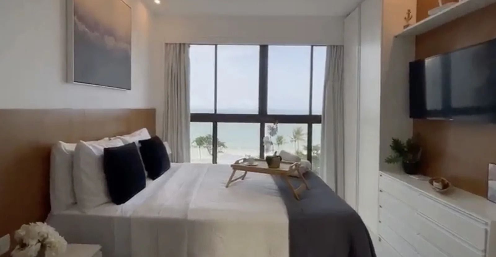 Quarto de hotel com uma cama grande, televisão na parede e vista para a praia.