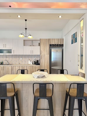 Cozinha moderna com ilha central, armários de madeira, geladeira de aço inoxidável e um lustre.