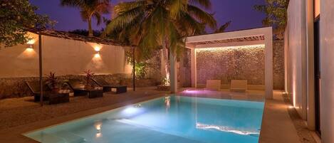 Piscina com espreguiçadeiras e uma parede de pedra.