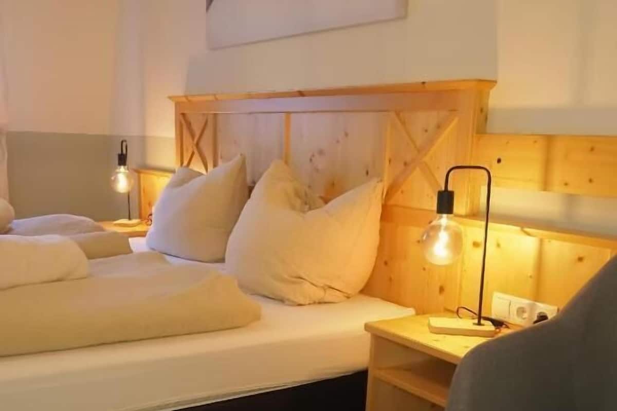 Um quarto acolhedor com cama, mesas de cabeceira, uma mesa redonda e uma cadeira.