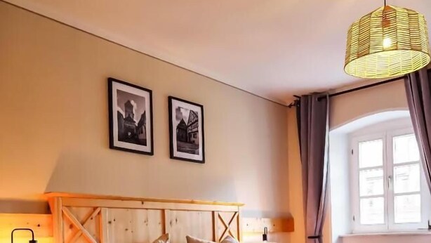 Quarto com cama de madeira, luminárias de cabeceira, janela com cortinas e duas quadros na parede.