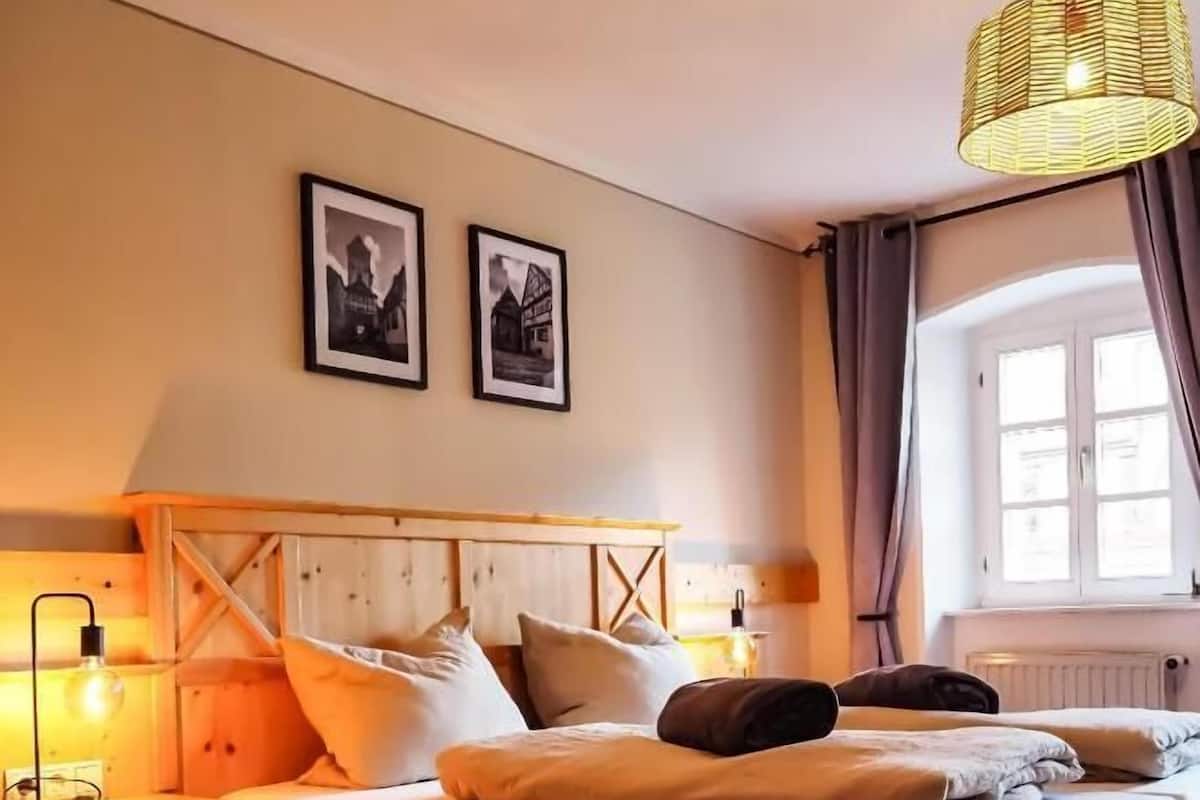 Quarto com cama de madeira, luminárias de cabeceira, janela com cortinas e duas quadros na parede.
