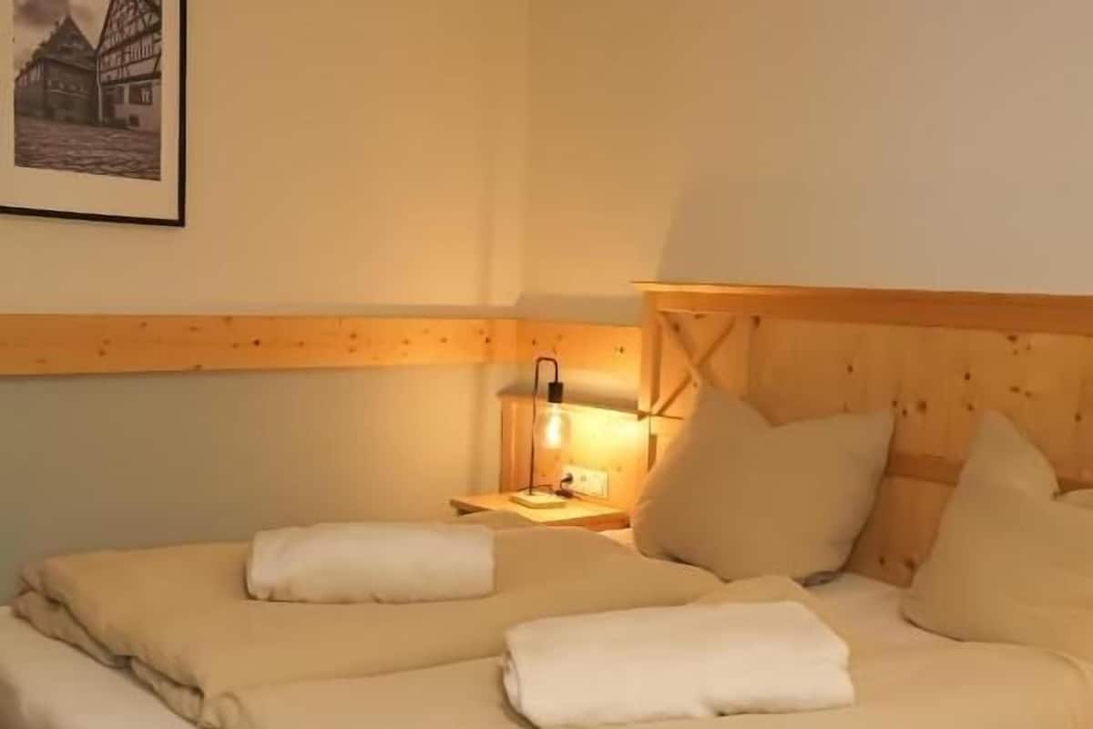 Quarto de hotel com cama, almofadas, mesa de cabeceira com abajur e um quadro na parede.
