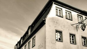 Um edifício com placa indicando ser um hotel, várias janelas e um caminho de tijolos que leva à entrada.