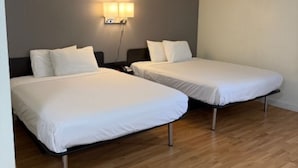 Quarto com duas camas de solteiro, luminária fixada na parede e piso de madeira.
