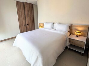 Quarto de hotel com cama grande, guarda-roupa de madeira, mesas de cabeceira com abajures e piso ladrilhado.