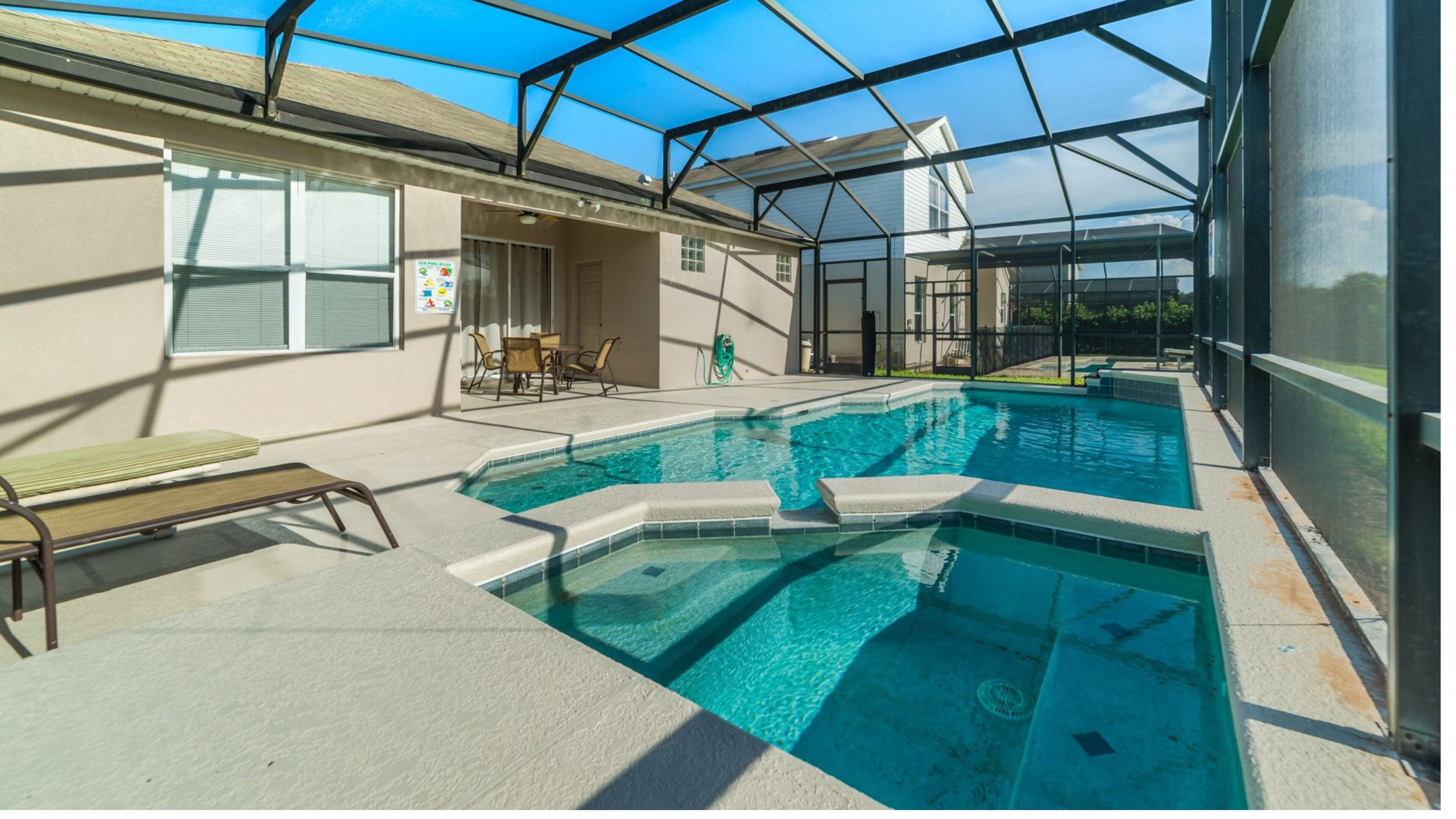 Piscina com cobertura de vidro, um banco e uma mesa com cadeiras.
