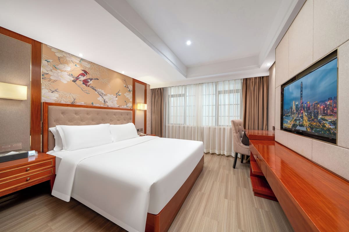 Quarto de hotel com uma cama grande, uma escrivaninha, uma televisão e vista para a cidade.
