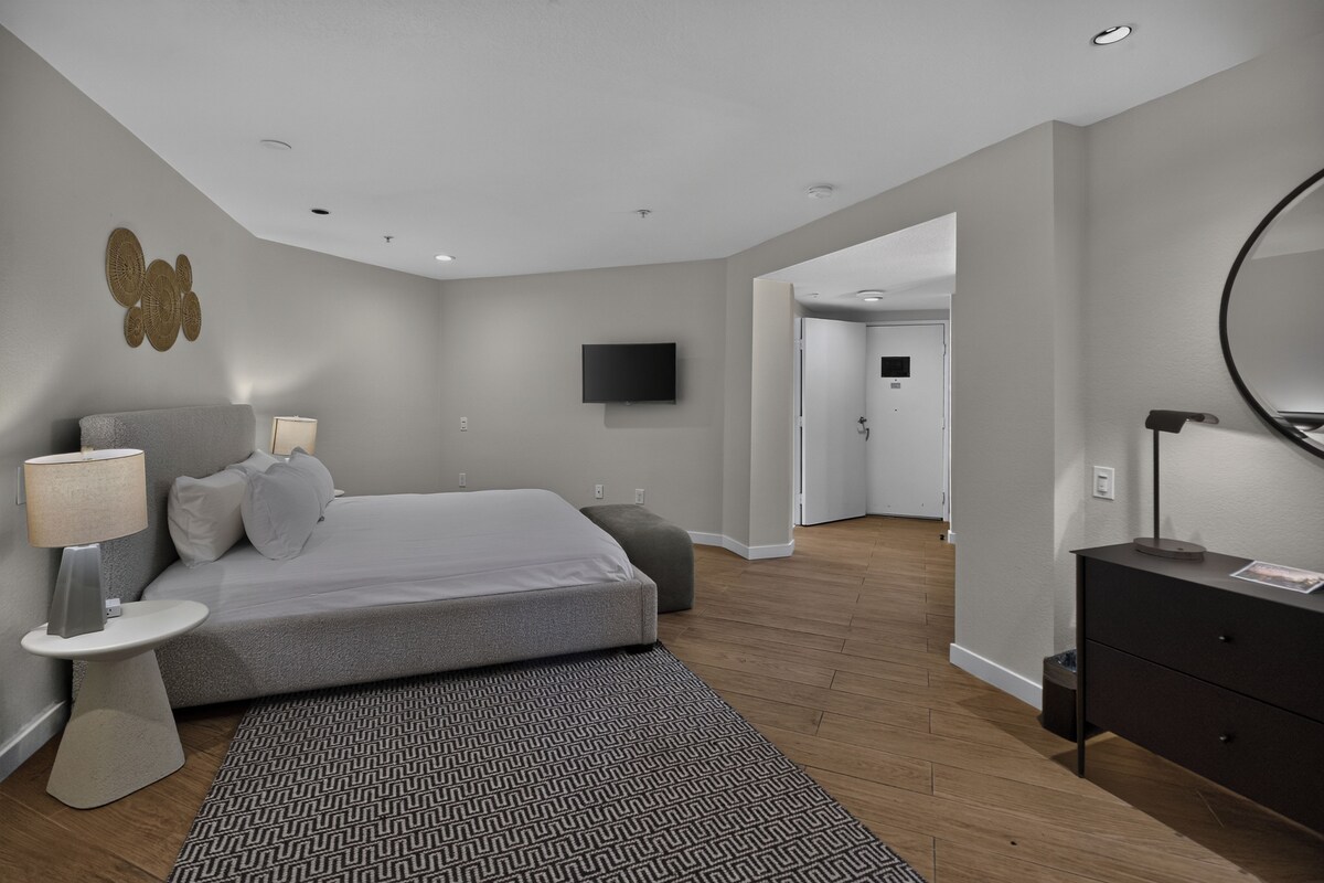 Quarto moderno com uma cama grande, abajures, televisão de tela plana, cômoda e espelho.