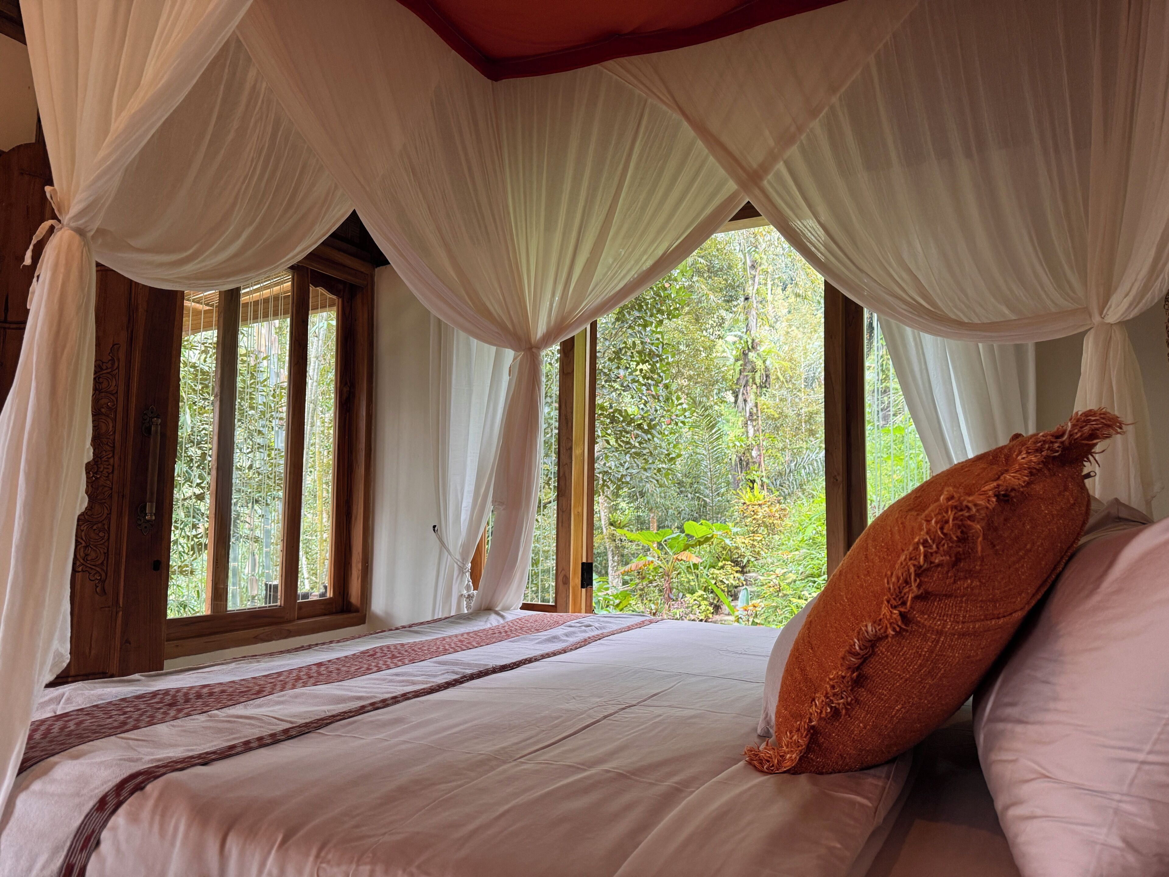 Quarto com cama de dossel, grandes janelas e vista para o verde lá fora.