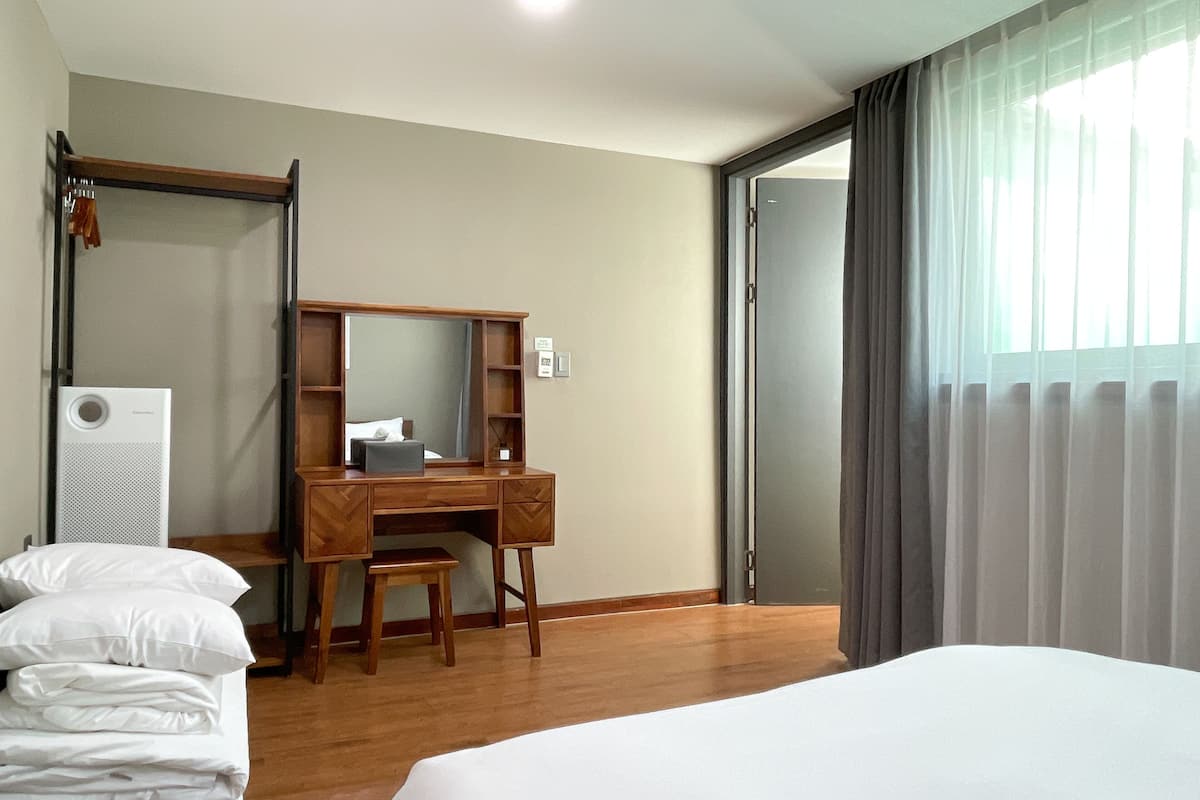 Quarto de hotel com cama, escrivaninha com espelho, cadeira, guarda-roupa e radiador.