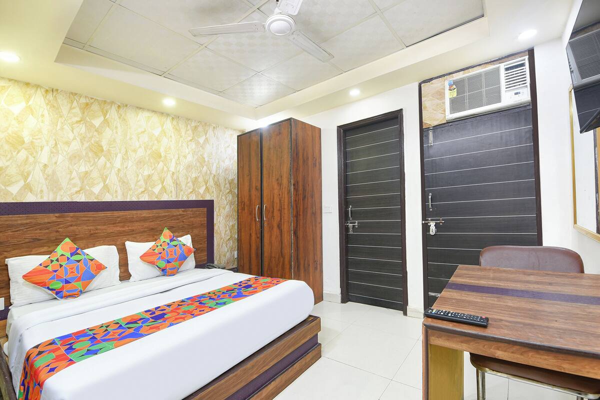 Quarto de hotel com cama, guarda-roupa, escrivaninha e ventoinha no teto.