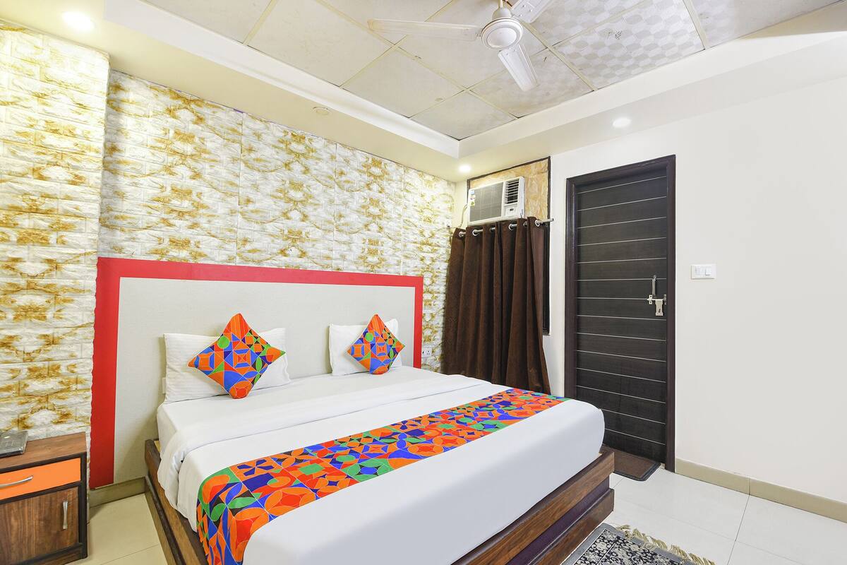 Quarto de hotel com cama, mesa de cabeceira, ar condicionado na parede, porta e ventoinha de teto.