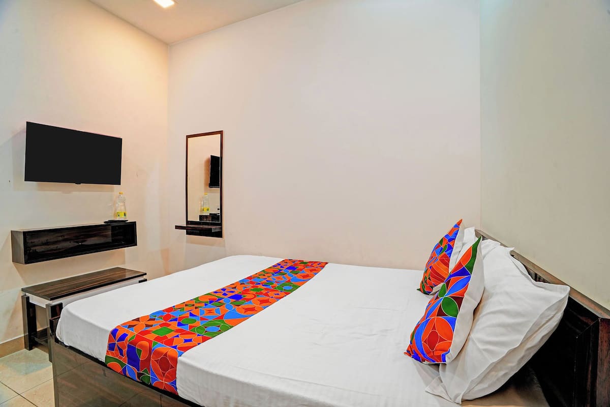 Quarto de hotel com cama, televisão na parede, mesa de cabeceira e espelho.