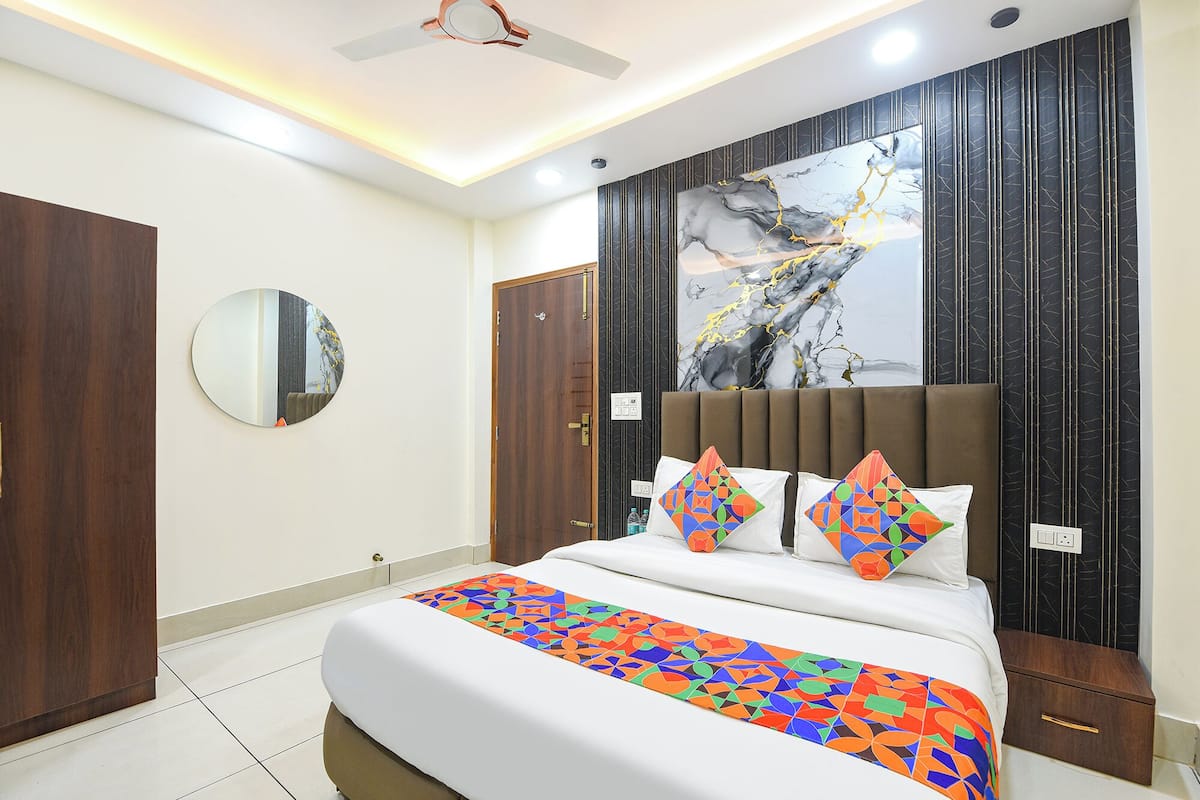 Quarto de hotel moderno com uma cama grande, um espelho redondo, um ventilador de teto e uma parede com padrão marmorizado.