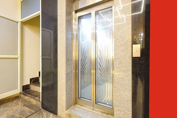Um elevador moderno com portas de vidro e interior metálico, próximo a uma escadaria de mármore.