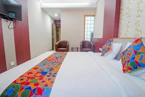 Quarto de hotel com uma cama, duas cadeiras, televisão e janela.