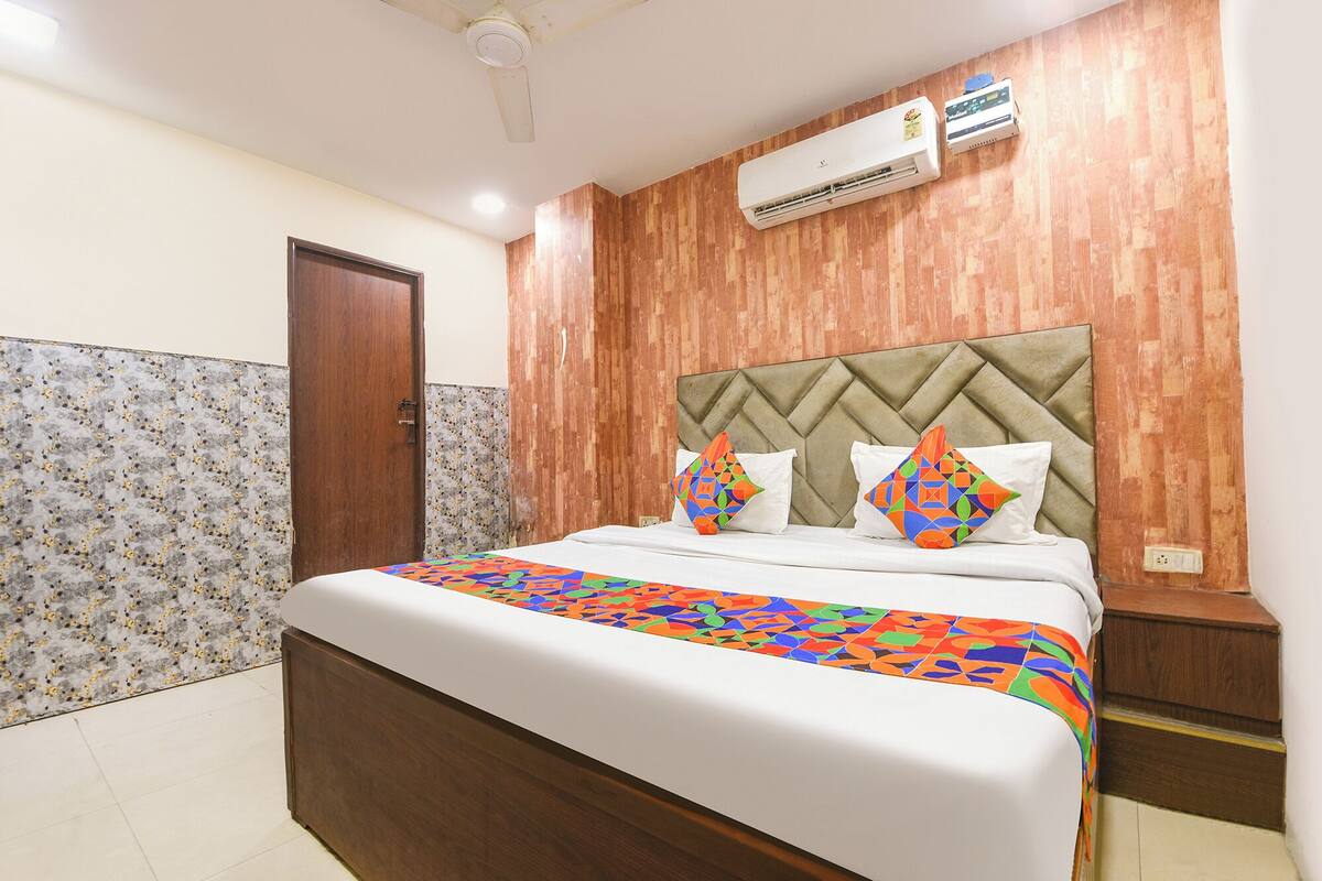 Quarto de hotel com cama, painel de parede de madeira, ar condicionado e uma porta.