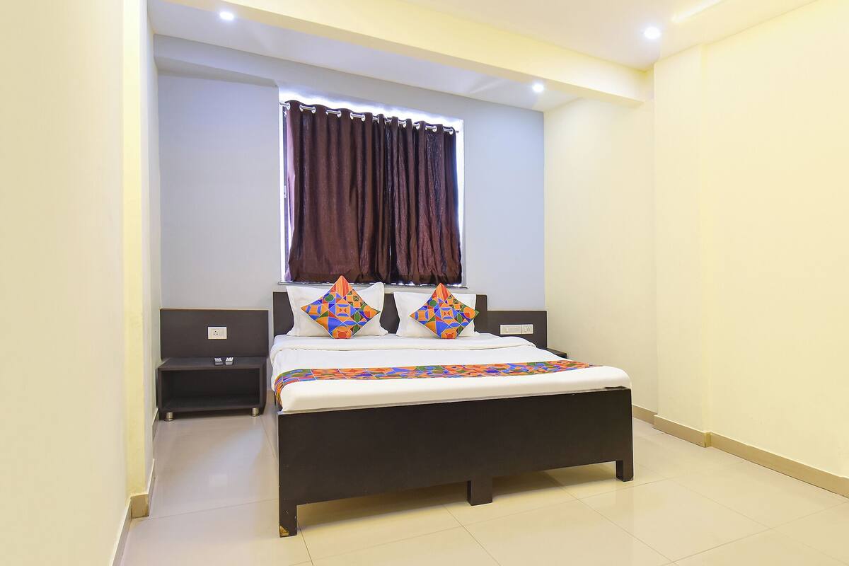 Quarto com cama, duas mesas de cabeceira, janela com cortinas e piso de azulejos.