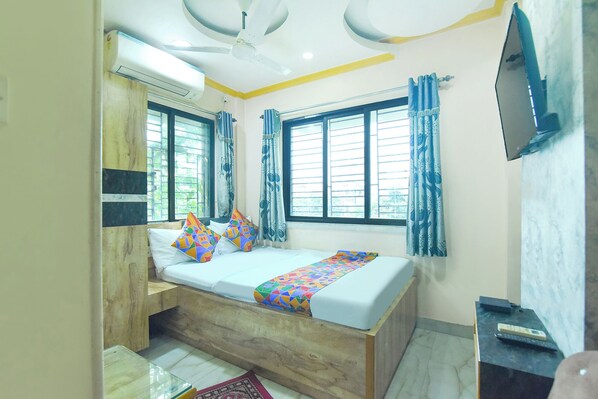 Quarto com cama, ventilador de teto, televisão e janelas com cortinas.