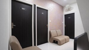 Quarto de hotel com três portas escuras, numeradas 101, 102 e 103, um sofá bege e um ventilador.