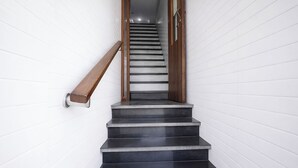 Uma escadaria com corrimão de madeira e degraus pretos, conduzindo a uma porta no topo.