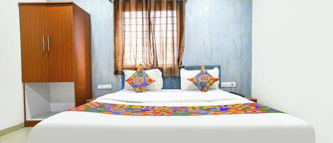 Quarto com cama, duas almofadas, guarda-roupa de madeira, janela com cortinas e parede com padrão floral.