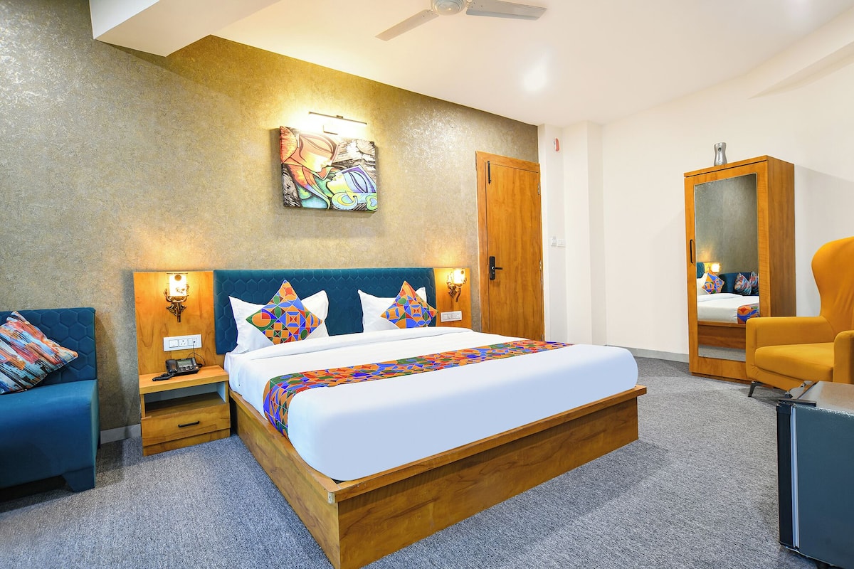 Quarto de hotel com cama, mesa de cabeceira, sofá azul, guarda-roupa de madeira e espelho.